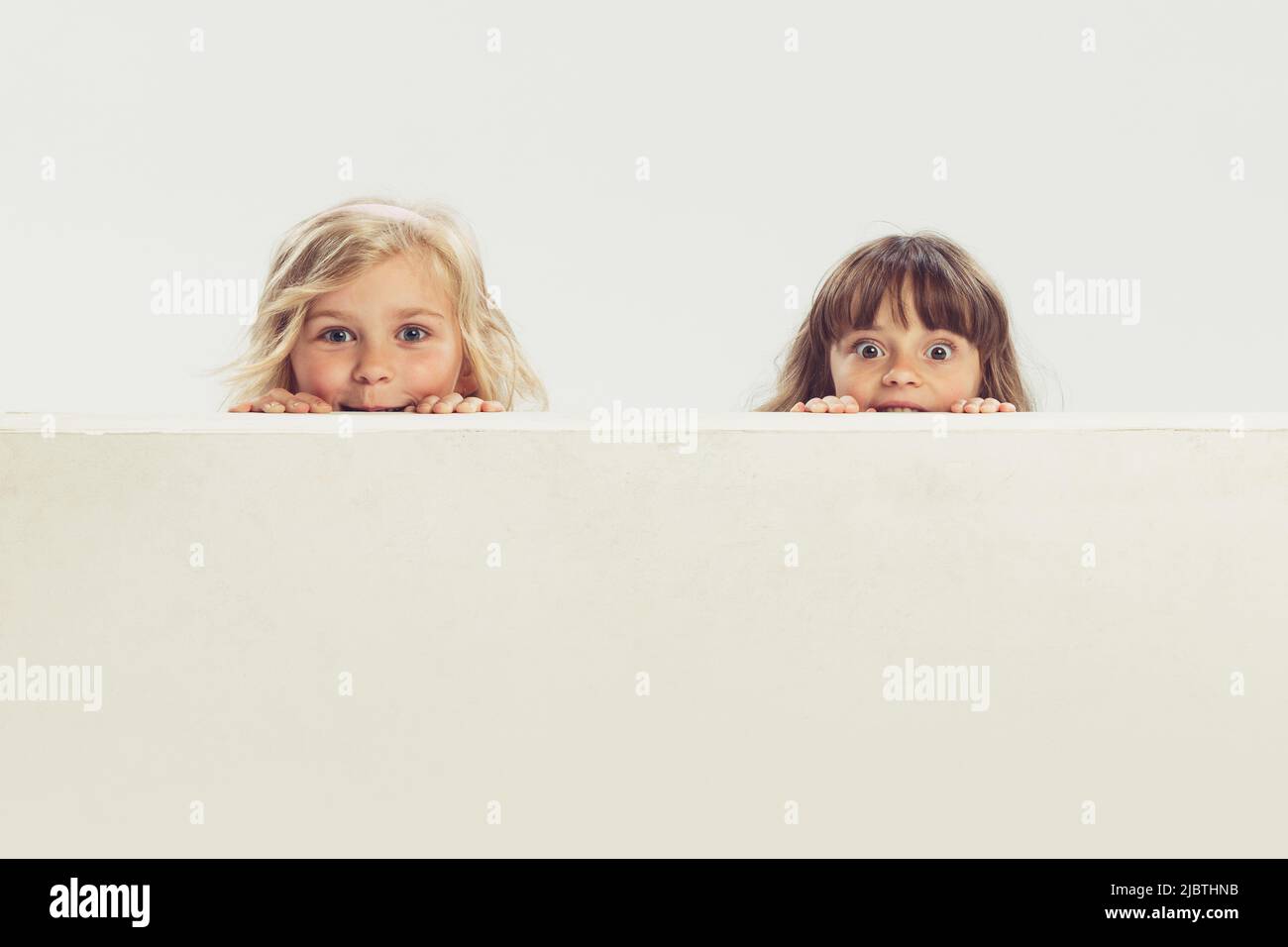 Portrait of two little beautiful girls, children peeking out the table ...