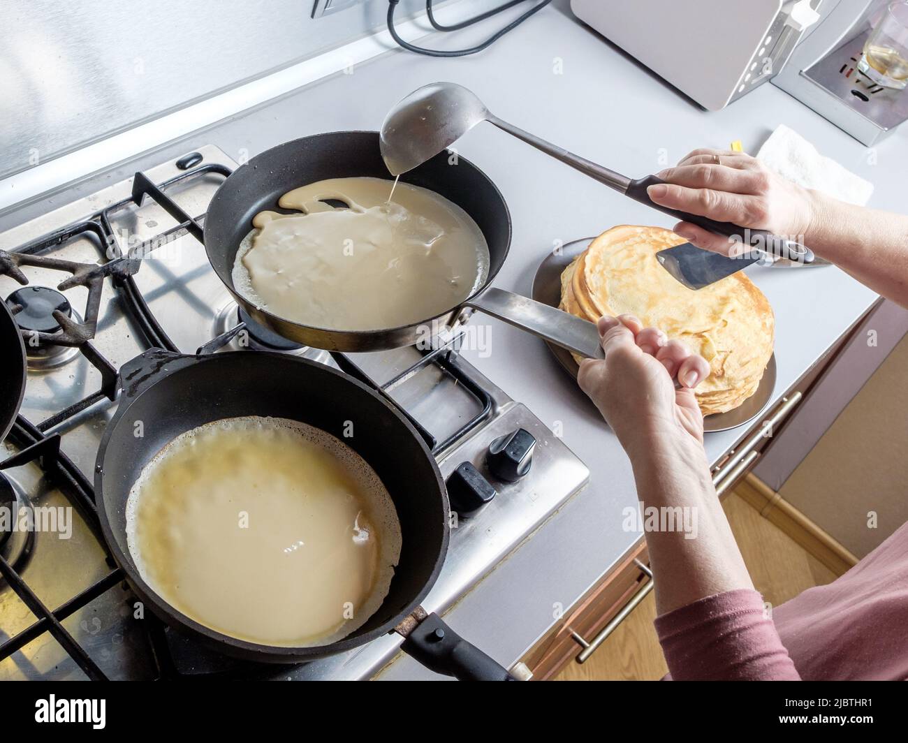 Batter pouring out of a metal bucket onto a red-hot greased frying pan ...
