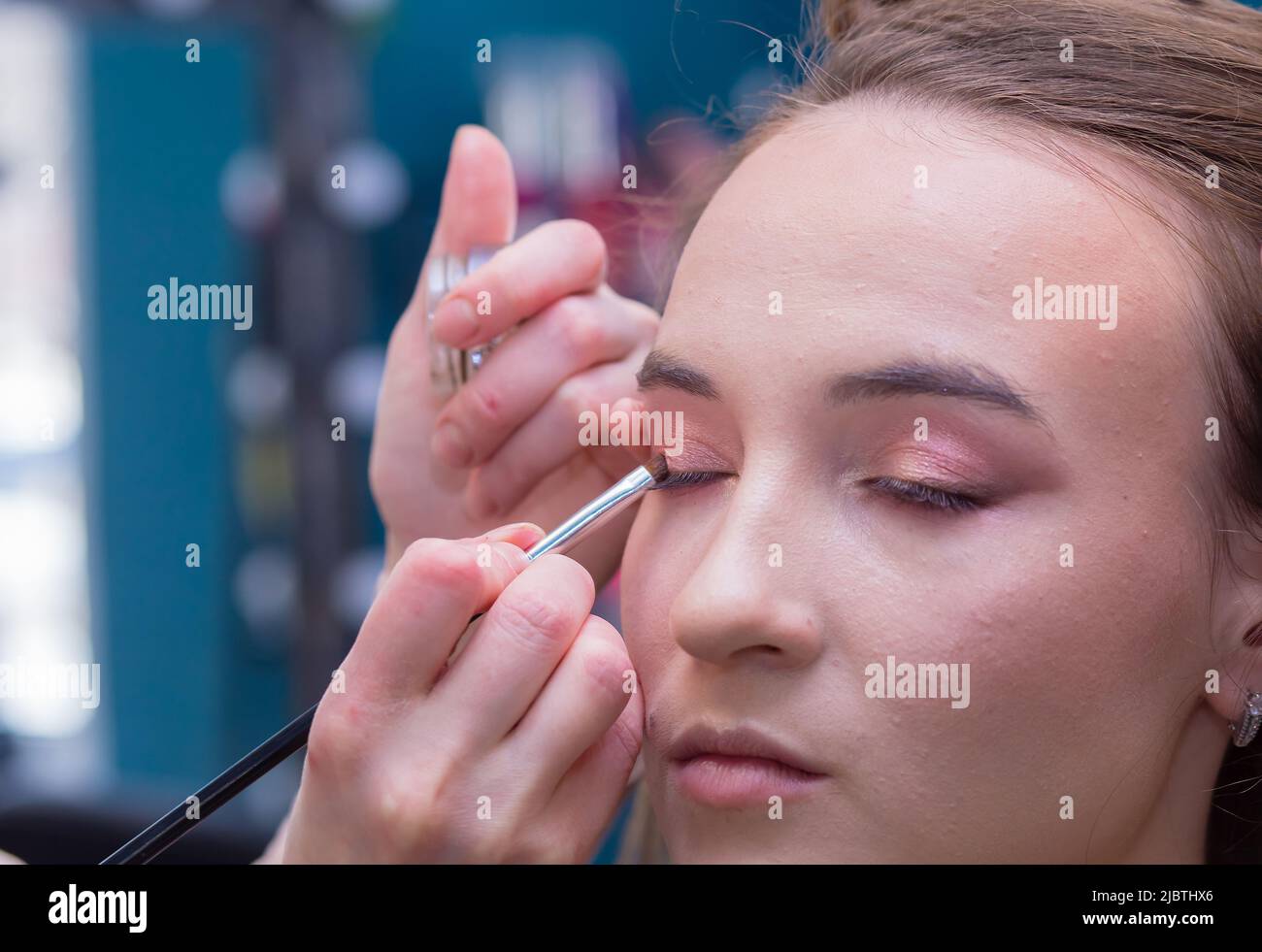 Close-up of a makeup artist's hand with a brush paints the eyelid of a ...