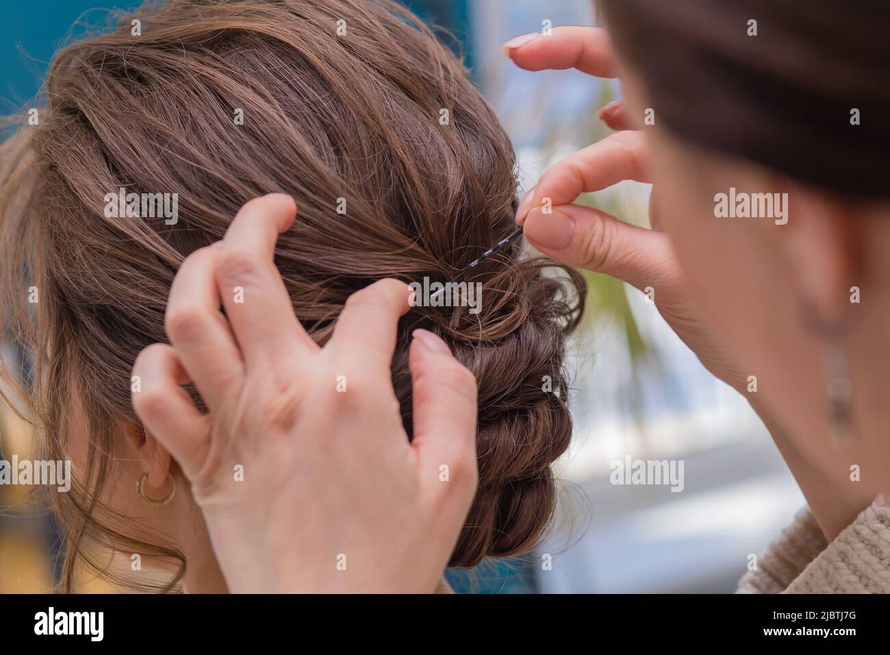 Women's fingers gently insert the hairpin into the client's hair. The ...