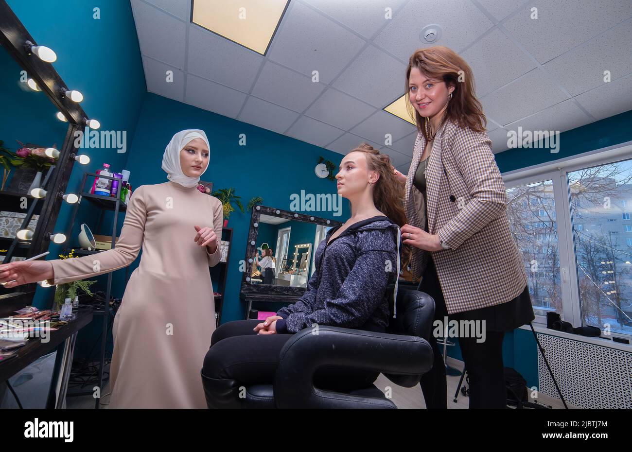 Woman masters with a smile style hair and make up a girl in a salon ...