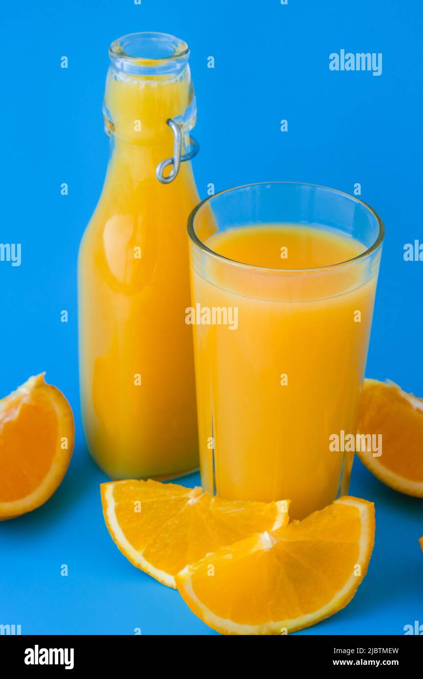 Glass bottle of fresh squeezing Orange juice with sliced fruits on blue ...