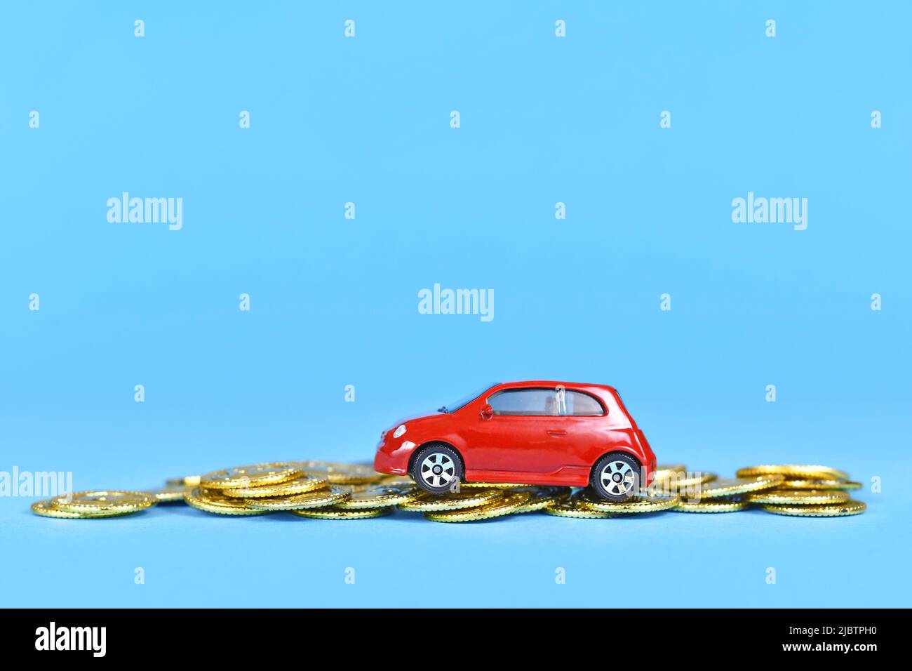 Small car driving on money coins on blue background with copy space ...