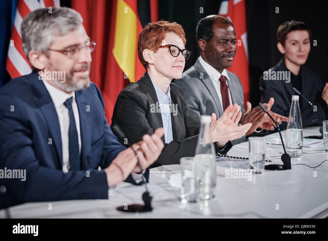 Group of politicians sitting at table and clapping hands during ...