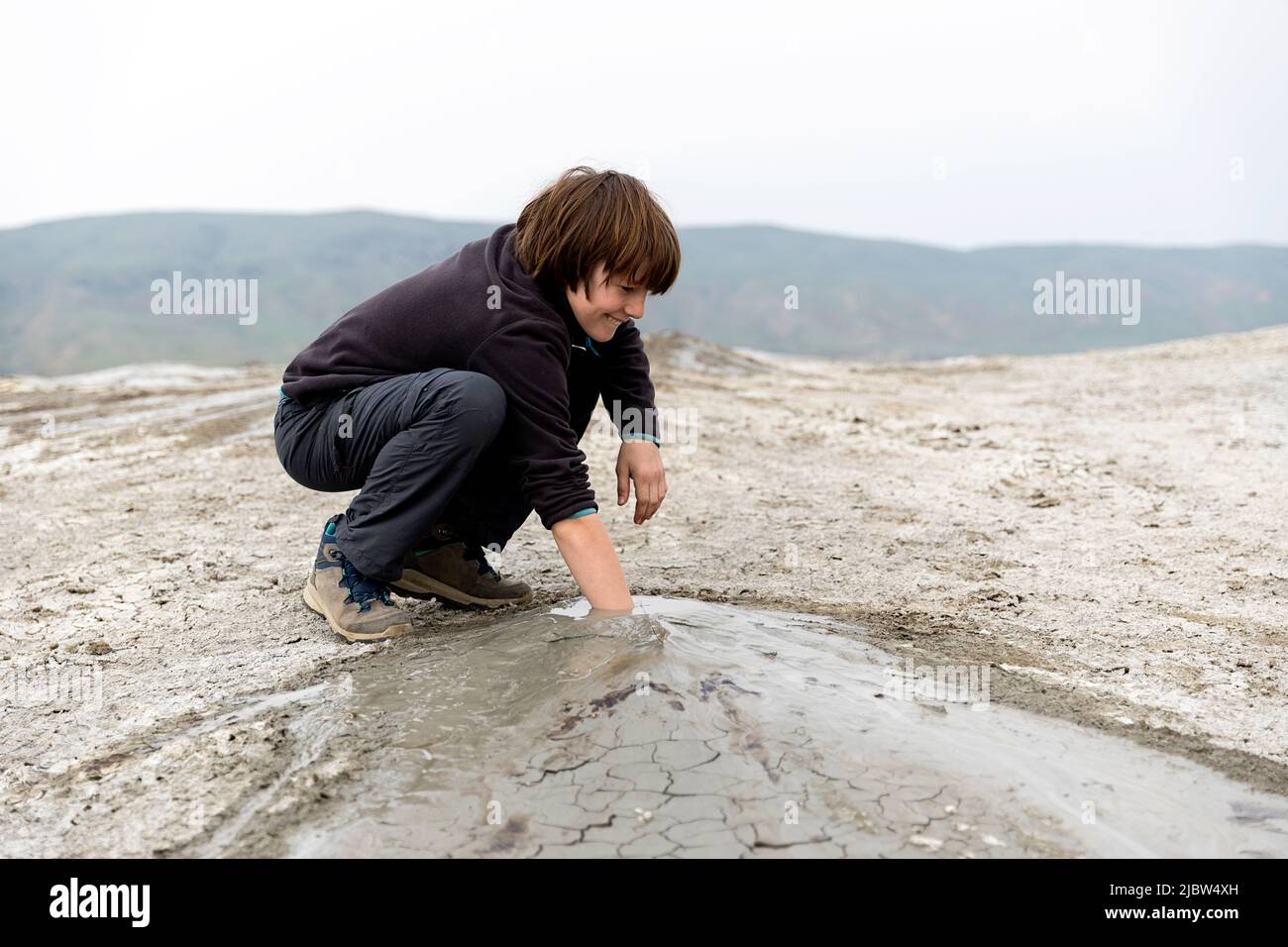 Smiling child putting hand into a mud volcano at Takhti-Tepha Mud ...