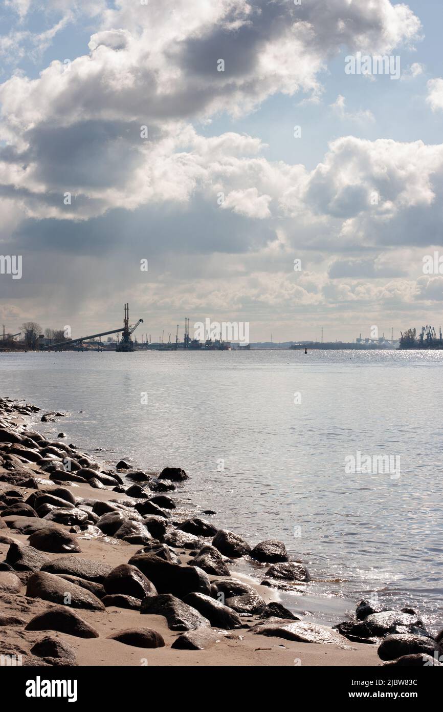 Rocky river bank landscape with a shipping port in the distance. the ...