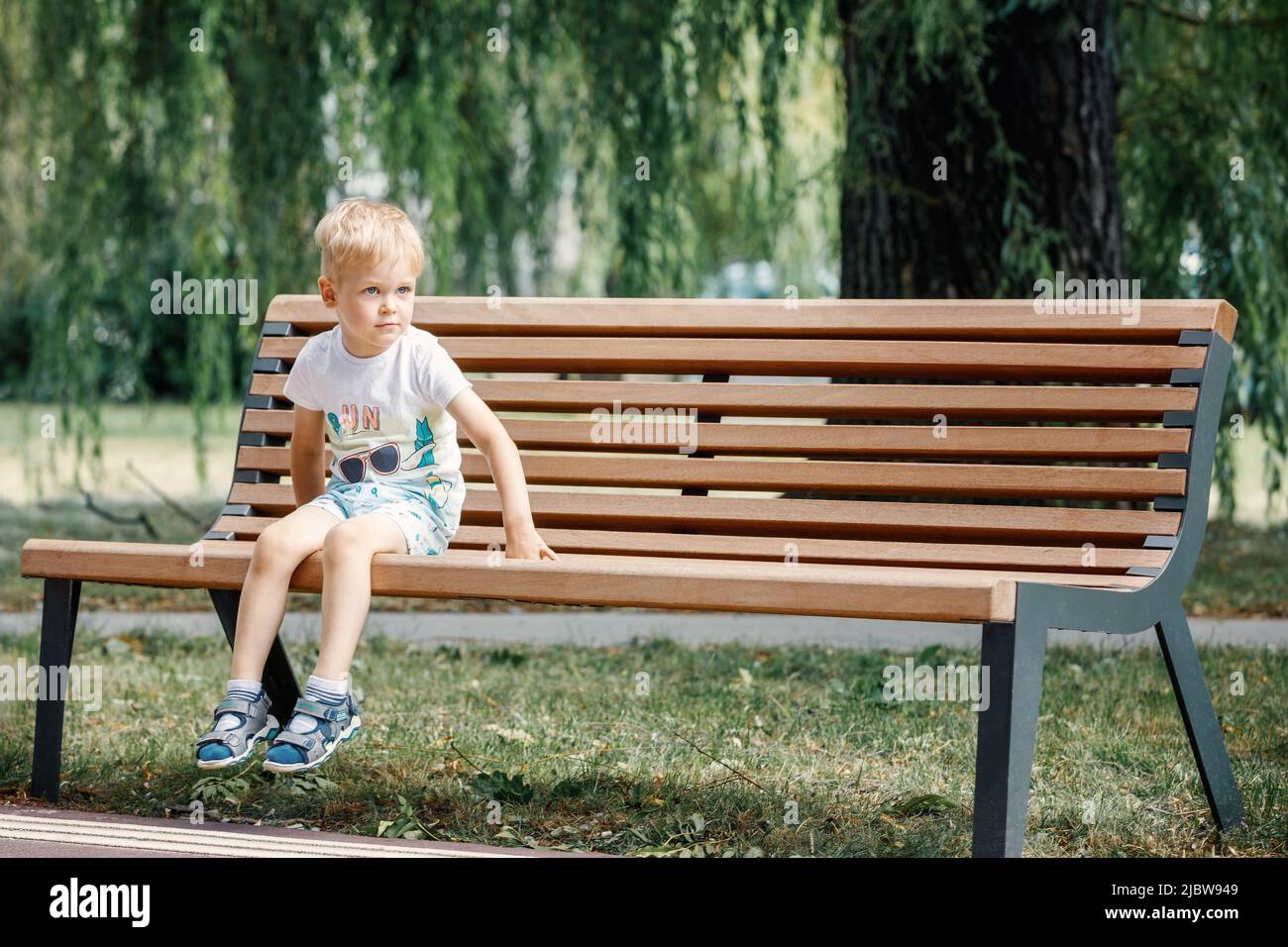 Small child plays in park, climbs onto bench.Kid is sitting on a park ...