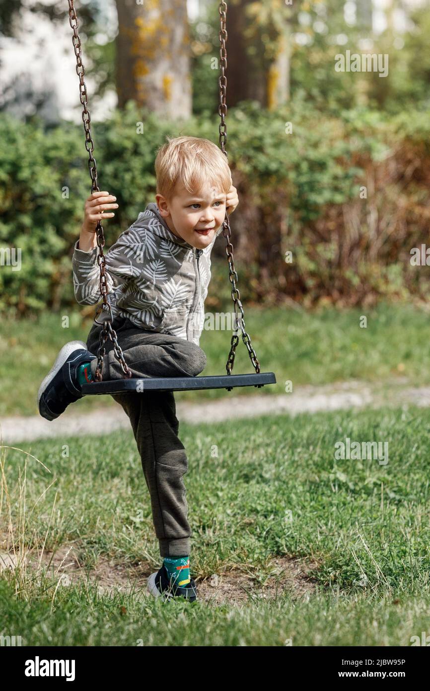 A little self-sufficient boy tries his best to climb a chain swing in a ...