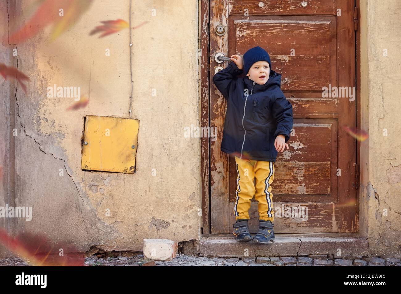 A little boy poses on an autumn day at the ancient door and cracked ...