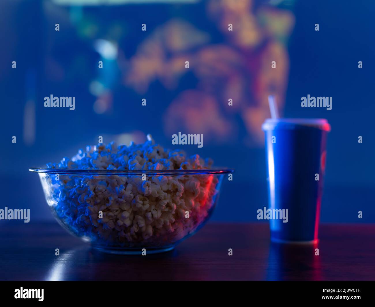 Popcorn in a glass bowl and a drink in a plastic glass with a straw ...