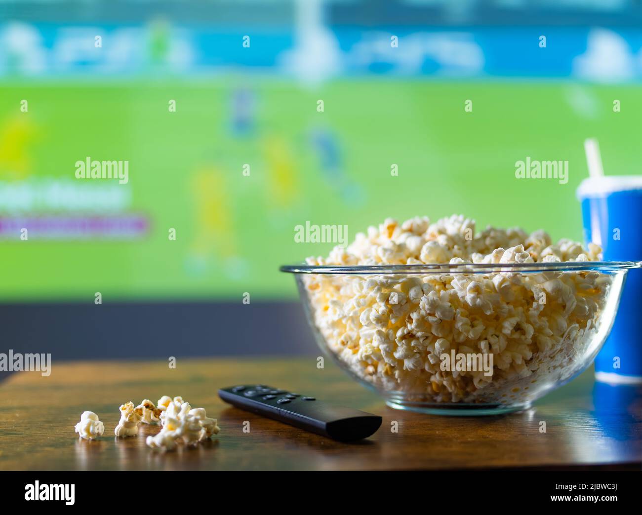 Popcorn in a glass bowl on the table and a TV remote control against ...