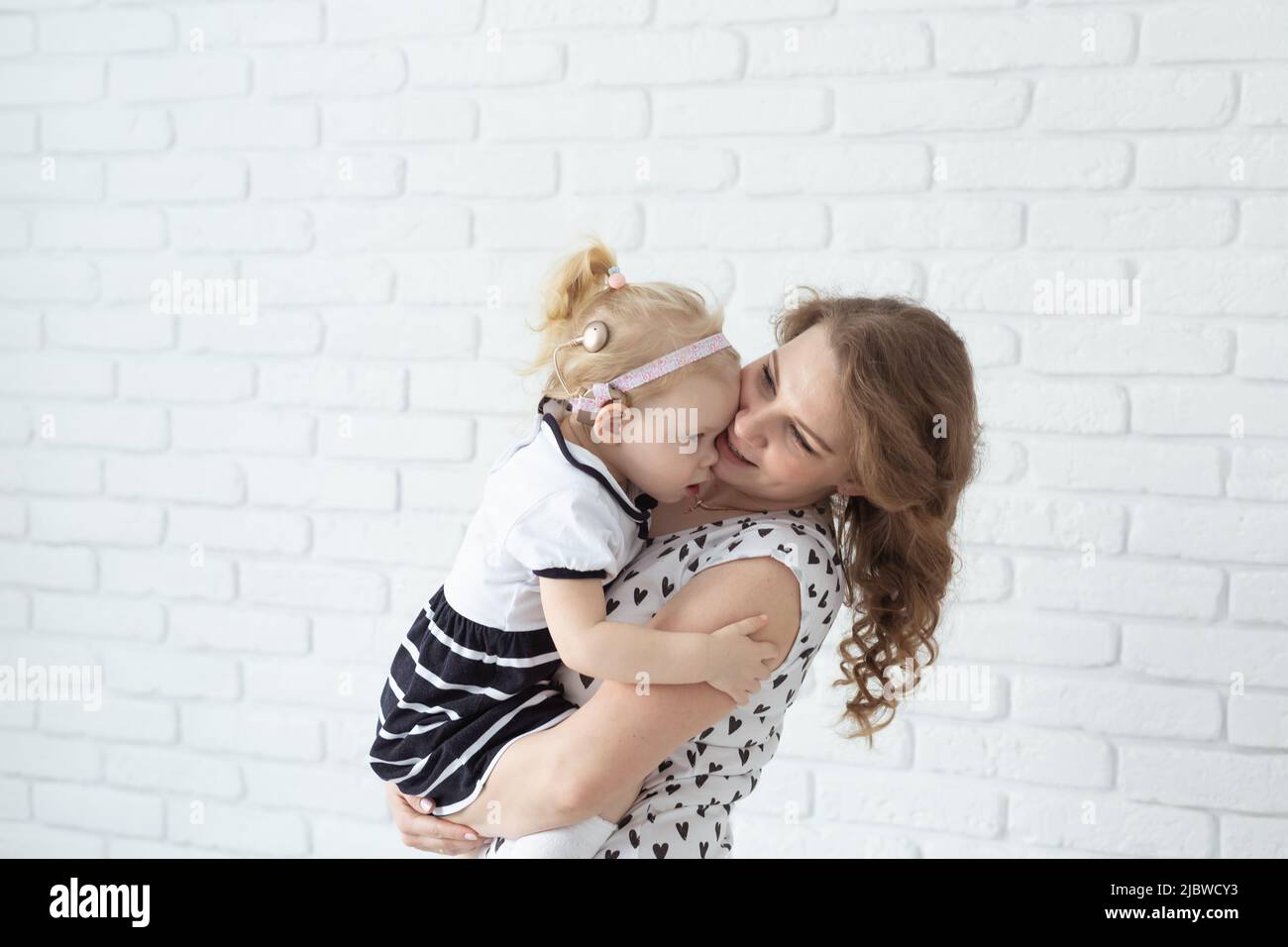 Mother holds her child with hearing aids and cochlear implants on white ...