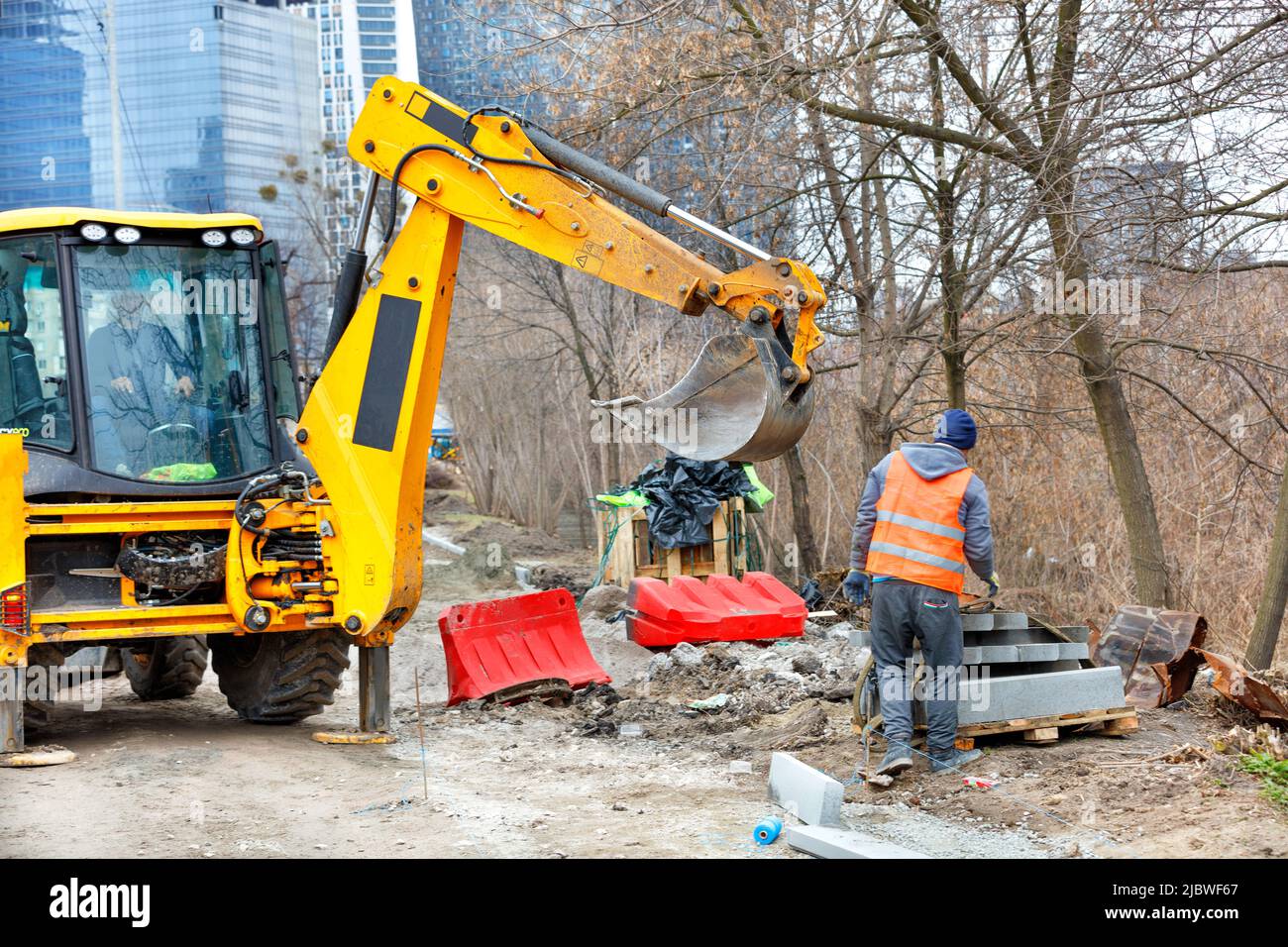 A group of construction workers unload concrete curbs with an excavator ...