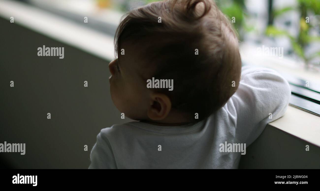 Baby boy standing by home window looking outside Stock Photo - Alamy