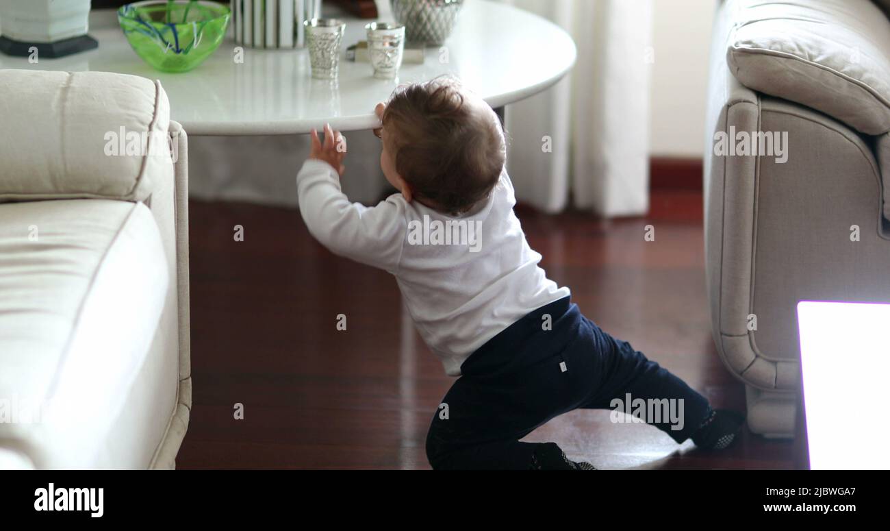 Baby learning to stand. Infant standing up holding into table furniture ...