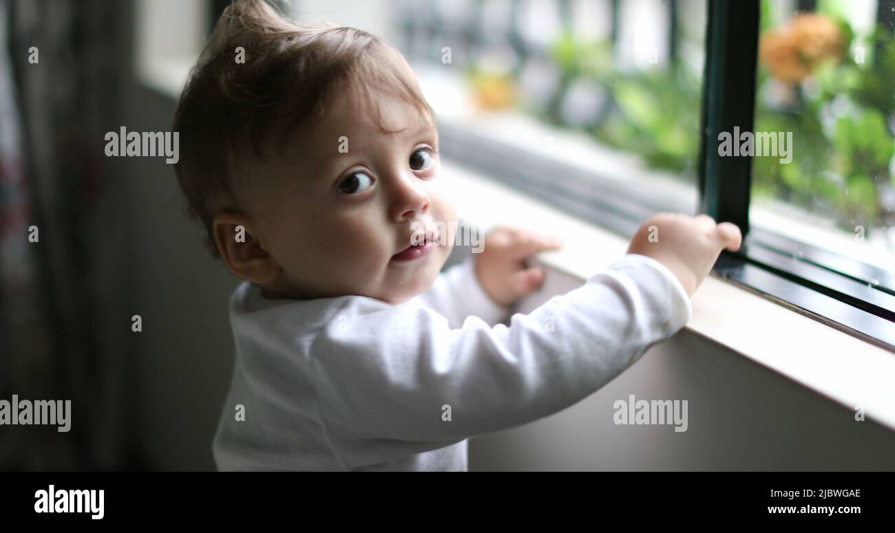 Baby next to home window looking outside. Infant boy leaning window ...
