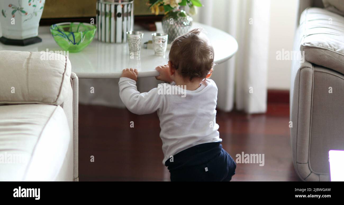 Baby learning to stand. Infant standing up holding into table furniture ...