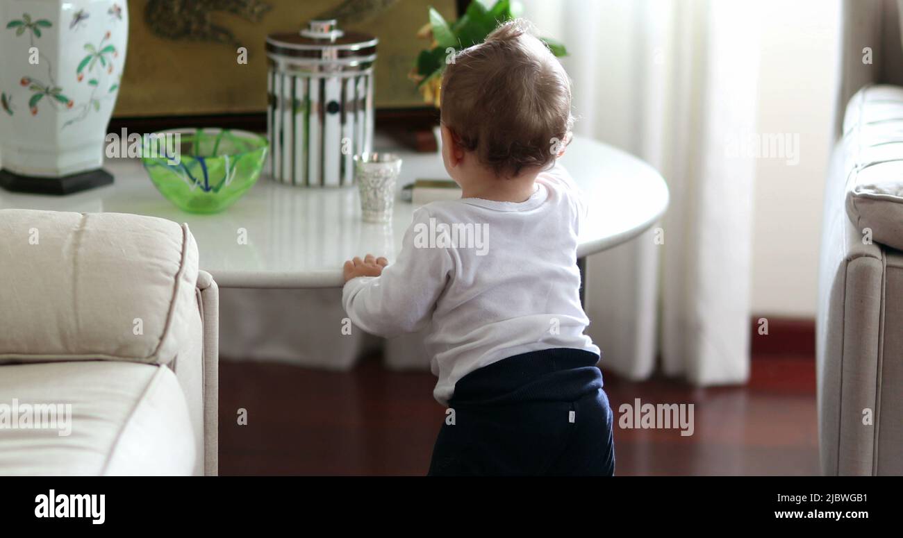 Baby learning to stand. Infant standing up holding into table furniture ...