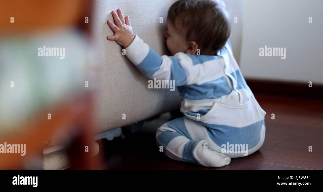 Baby learning to stand up by leaning on home sofa couch. Infant child ...