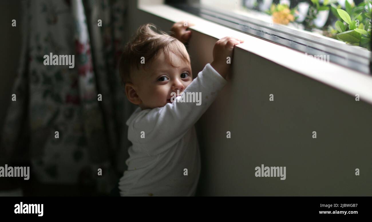 Baby next to home window looking outside. Infant boy leaning window ...