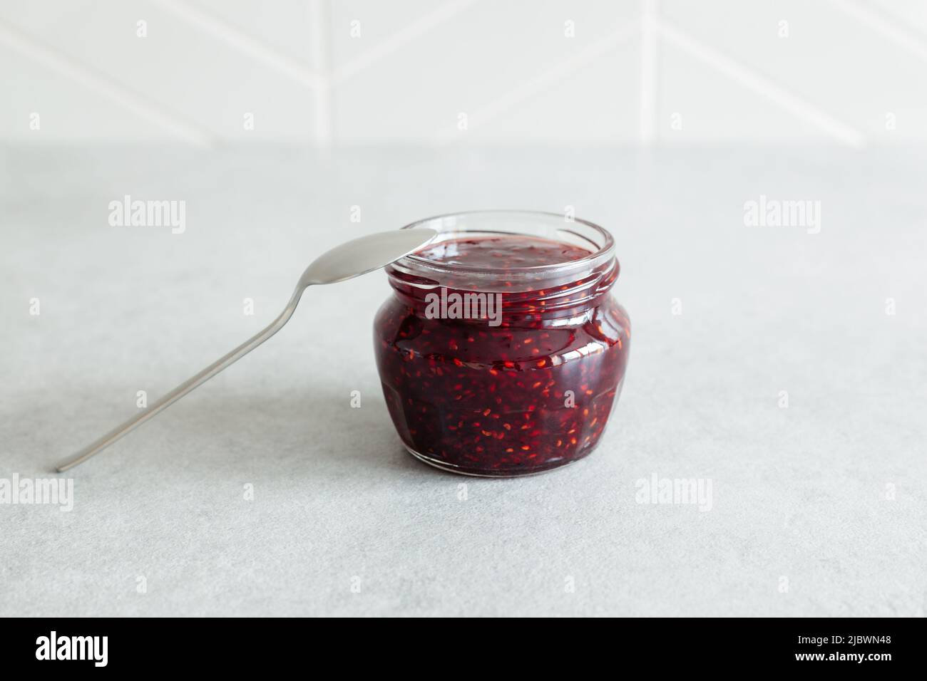 Natural homemade red raspberry jam in a small glass jar with spoon on ...