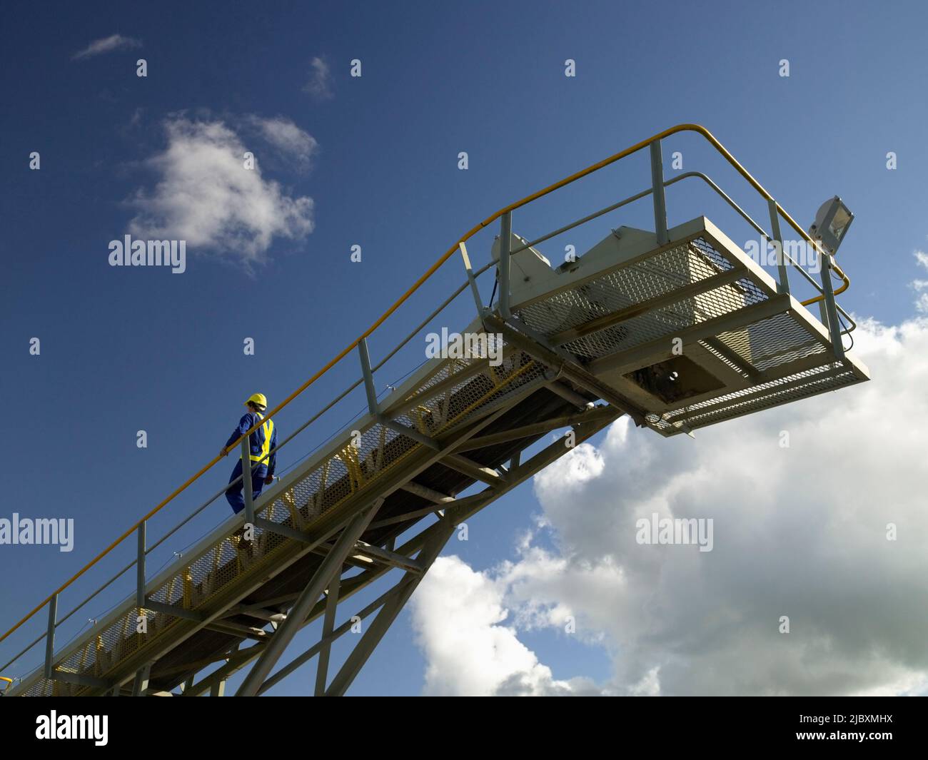 Man walking along raised conveyor belt against blue sky in quarry Stock ...