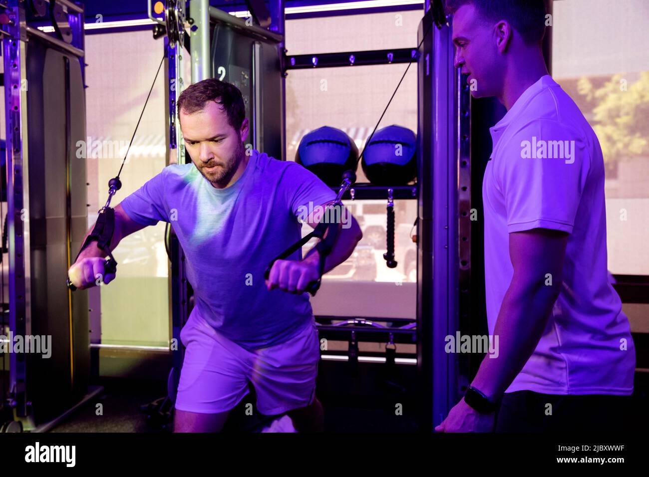 Gym owner helping male client with technique during workout in gym ...