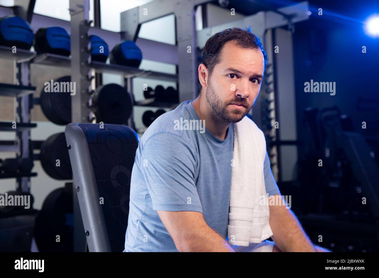 Male personal trainer sitting on weight bench after training client ...