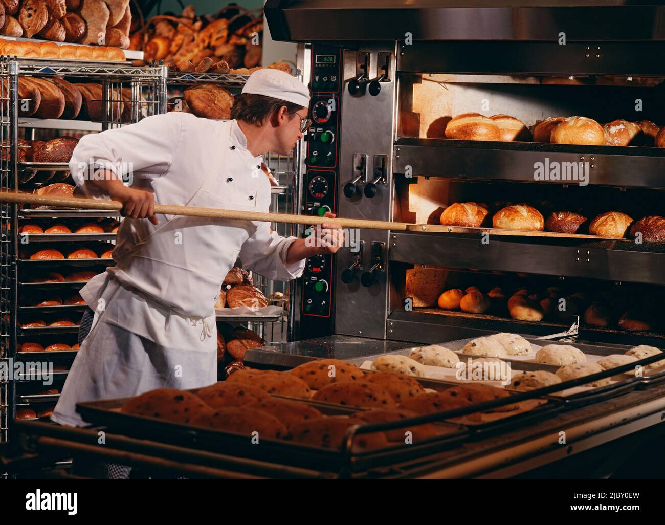 Baker feeding loafs of dough into industrial bakery oven Stock Photo ...
