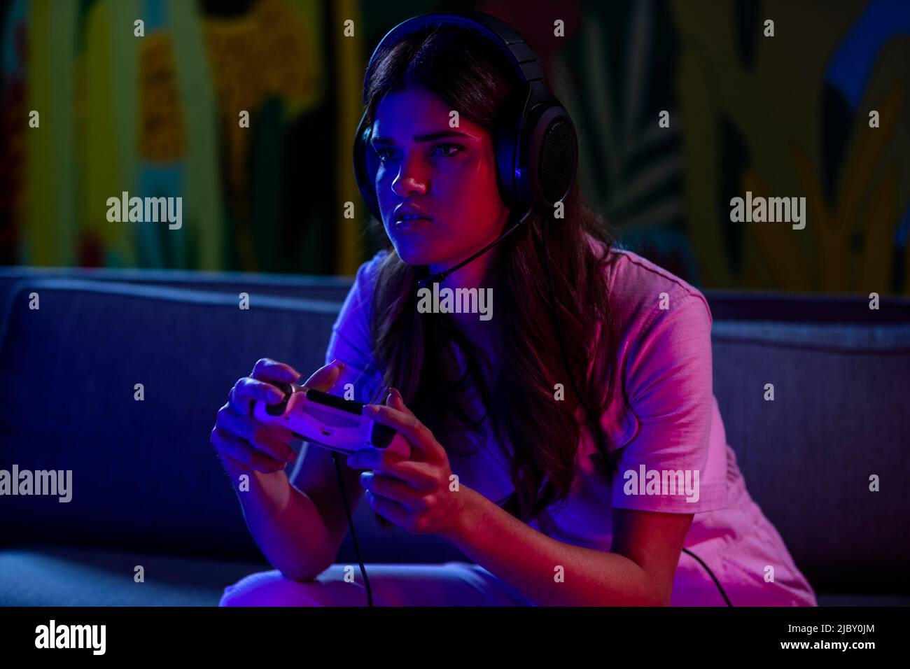 Female gamer playing video game sitting on couch in dark room Stock ...