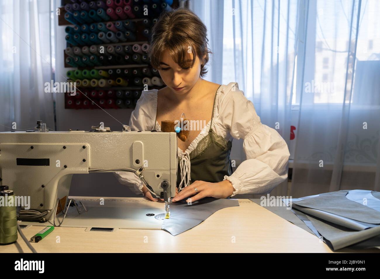 Young design studio owner female at workplace sew clothes on sewing ...