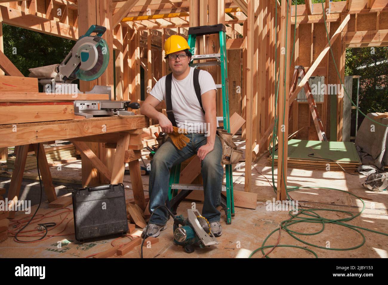 Man at a residential construction site sitting on a ladder and leaning ...