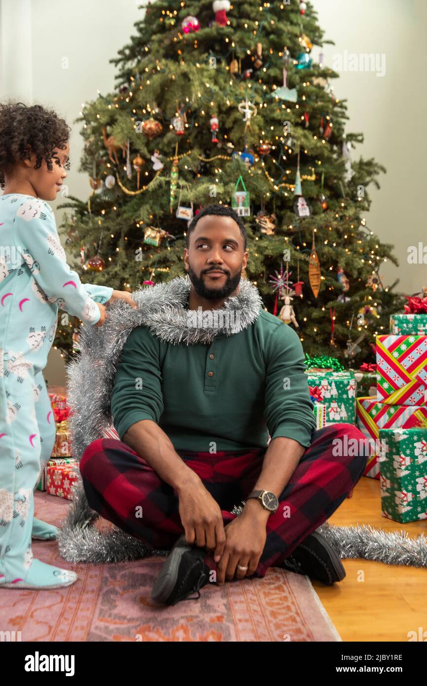 A little girl decorating her father with garland in front of Christmas ...
