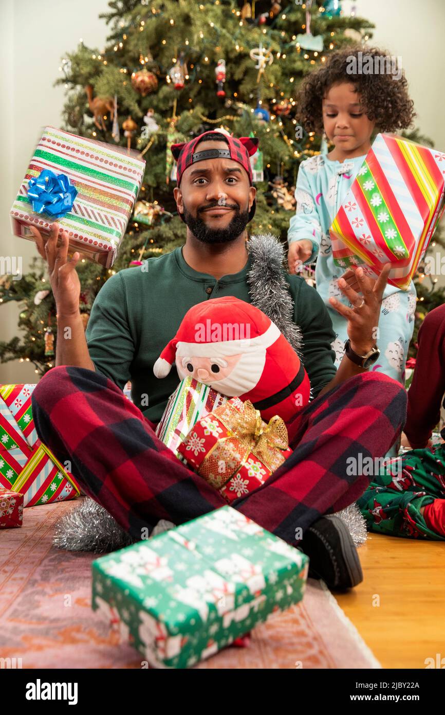 Father holding Christmas gift in each hand, looking into camera with ...