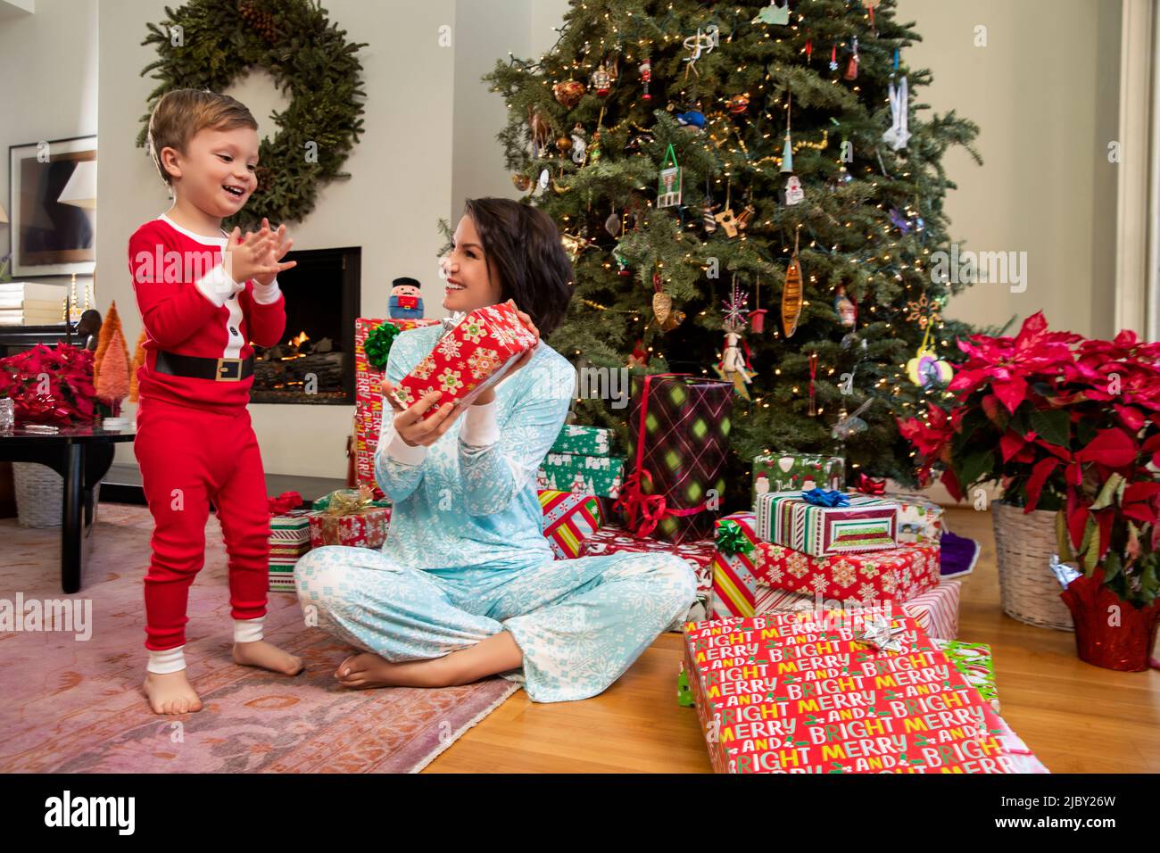 Boy in Santa pajamas clapping hands in excitement as mother hands him ...