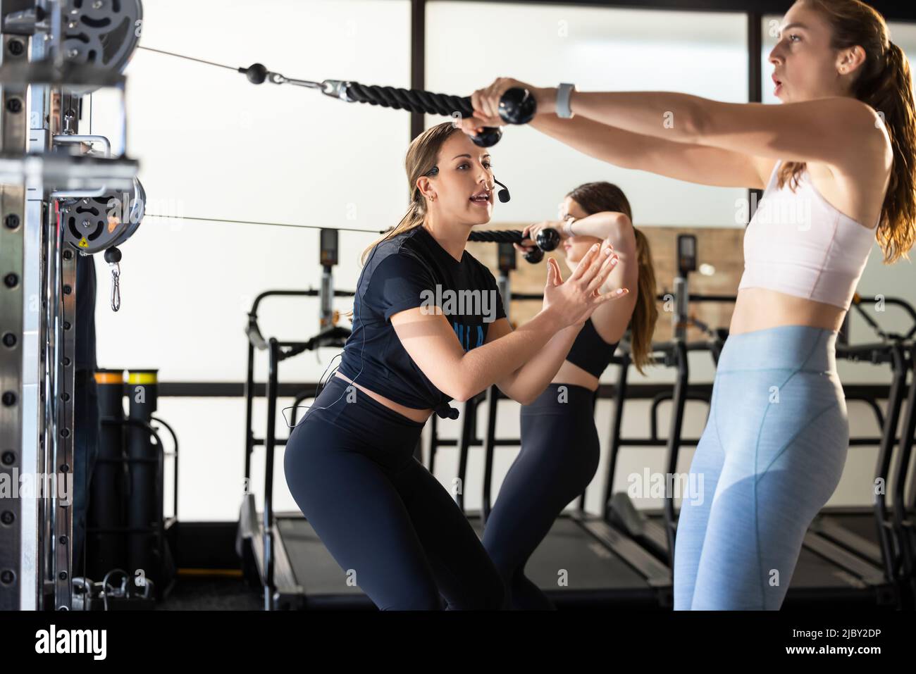 Female fitness instructor assisting woman in weight training class ...