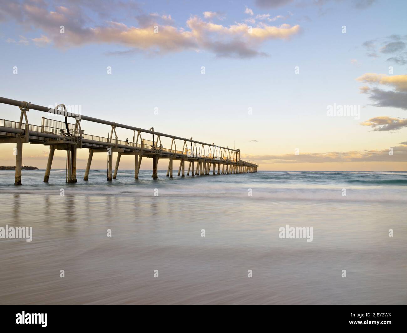 People walking and fishing on long jetty stretching out to sea in early ...