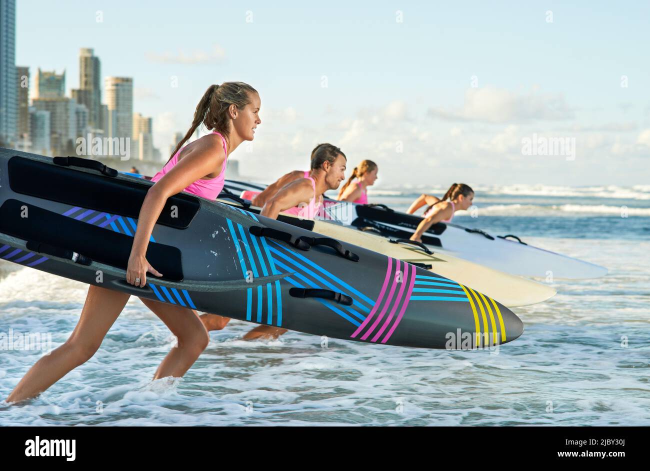 Mixed team of Surf Lifesavers holding surfskis and running into choppy ...
