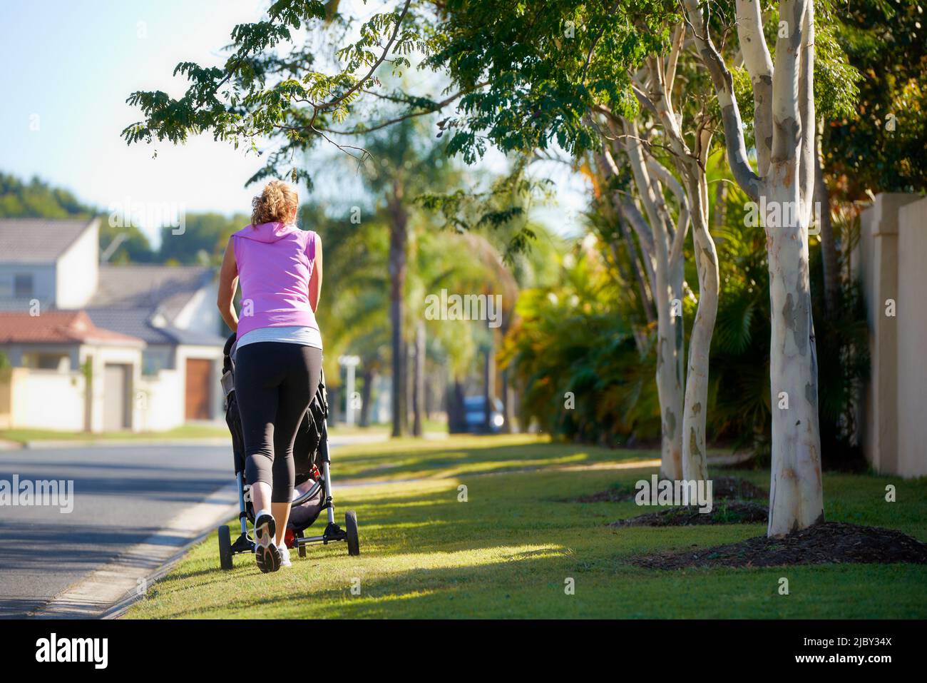 Back view of young mother pushing baby in stroller along urban street ...