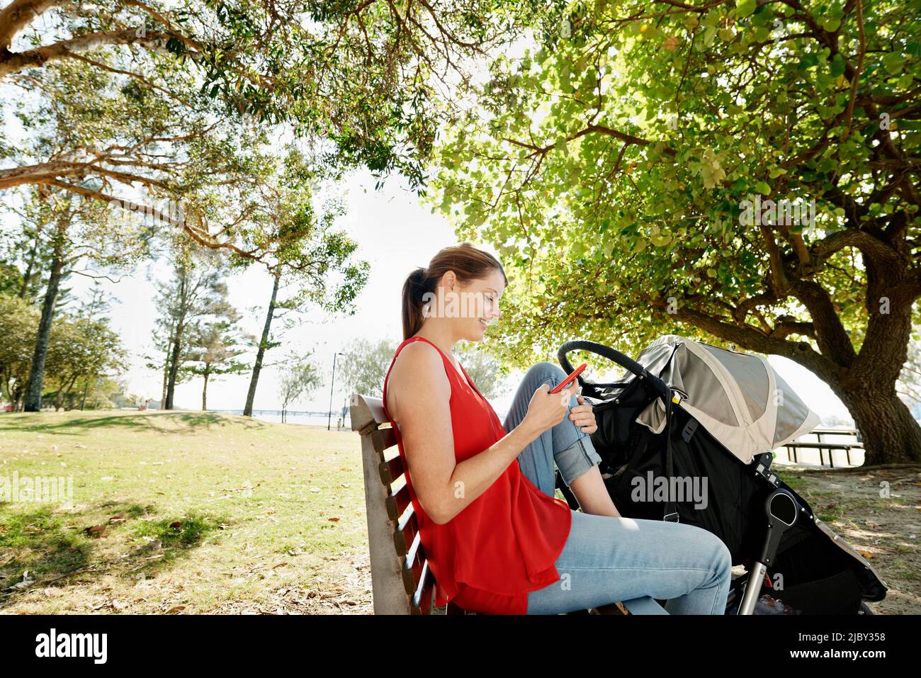 Young mother sitting on park bench with baby stroller Stock Photo - Alamy