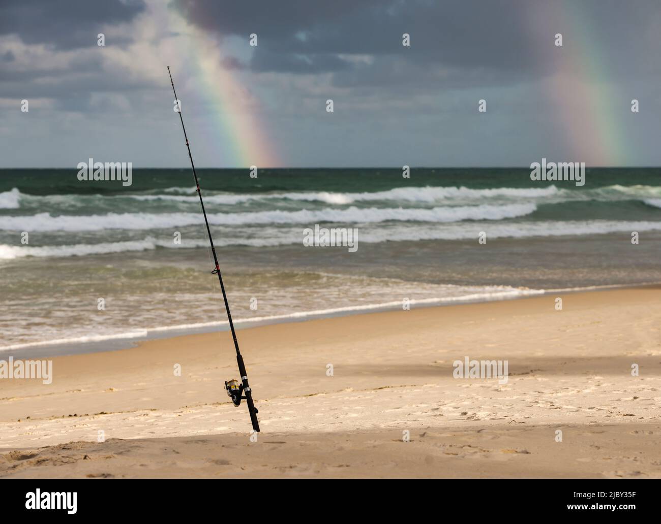 Surf caster fishing rod secured in the sand and double rainbow in ...
