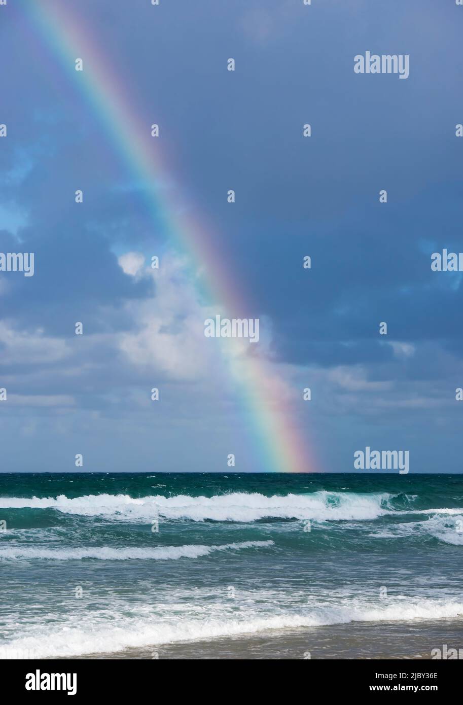 Rainbow shining in stormy sky as waves roll onto shore Stock Photo - Alamy