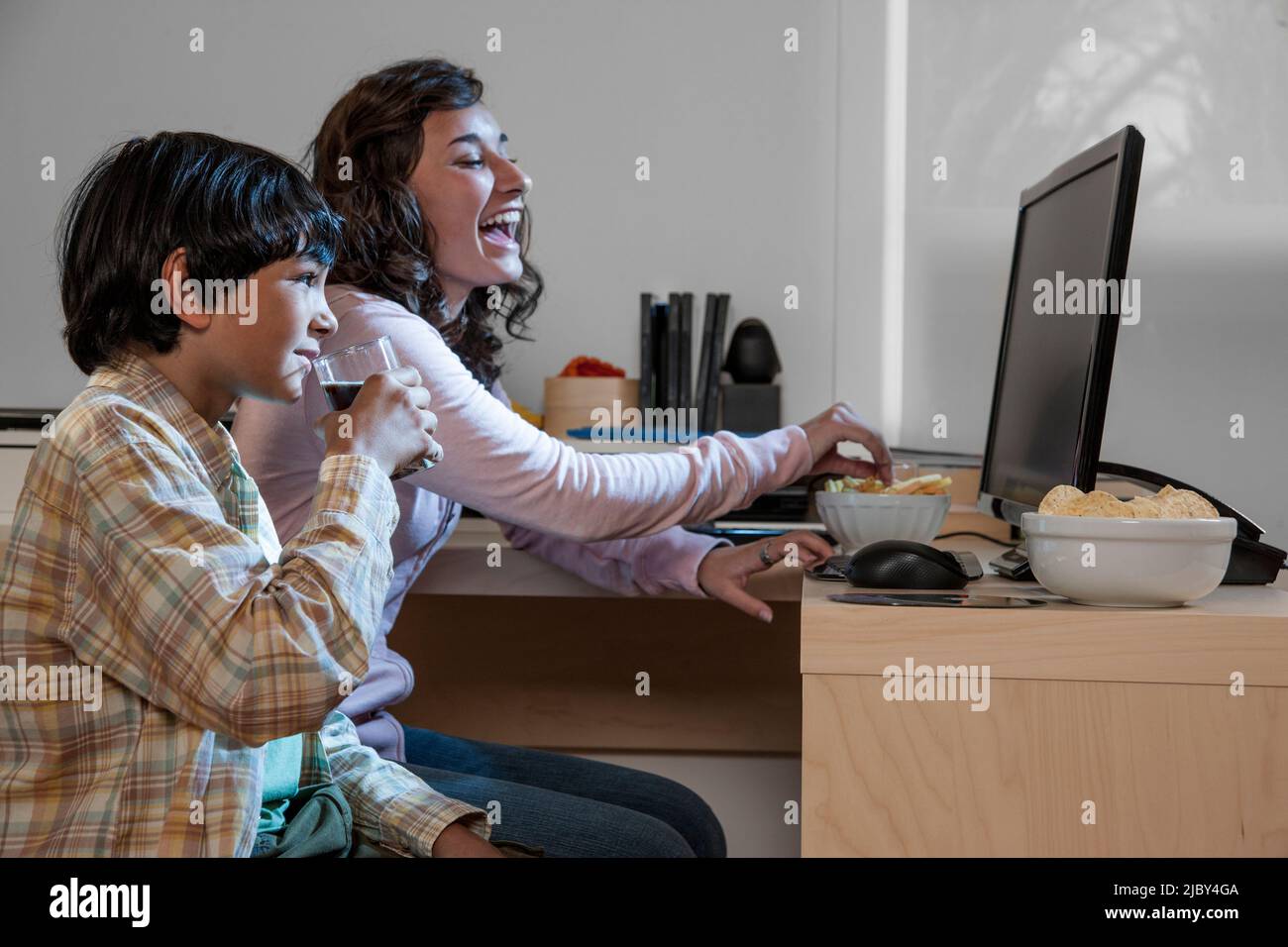 A brother and sister eating snack and watching a movie on a computer ...