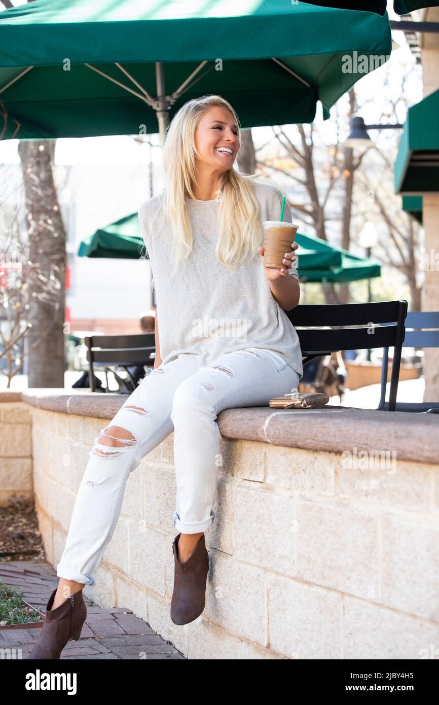 Woman at a cafe holding iced coffee looking back over her shoulder ...