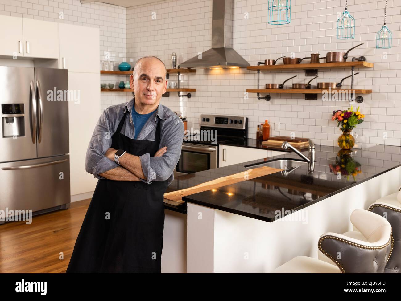 Man leaning against kitchen countertop with arms crossed looking into ...