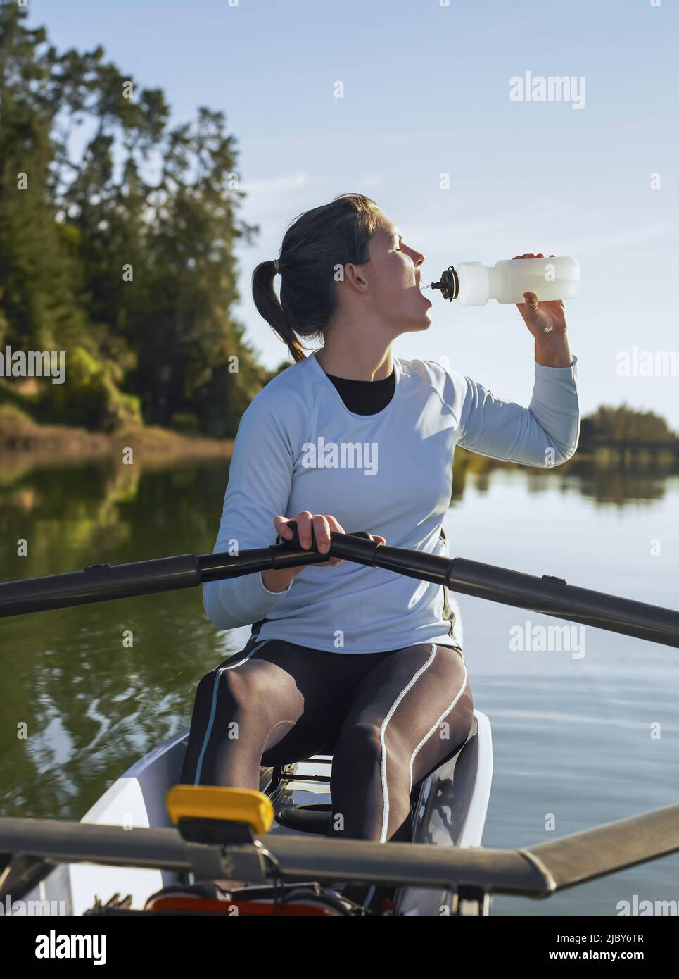 Female rower sitting in single scull canoe and drinking from bottle ...