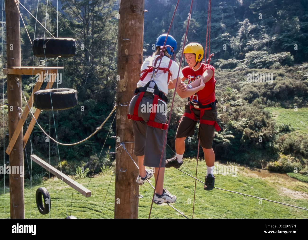 Two women helping each other balance on suspended ropes at outdoor ...