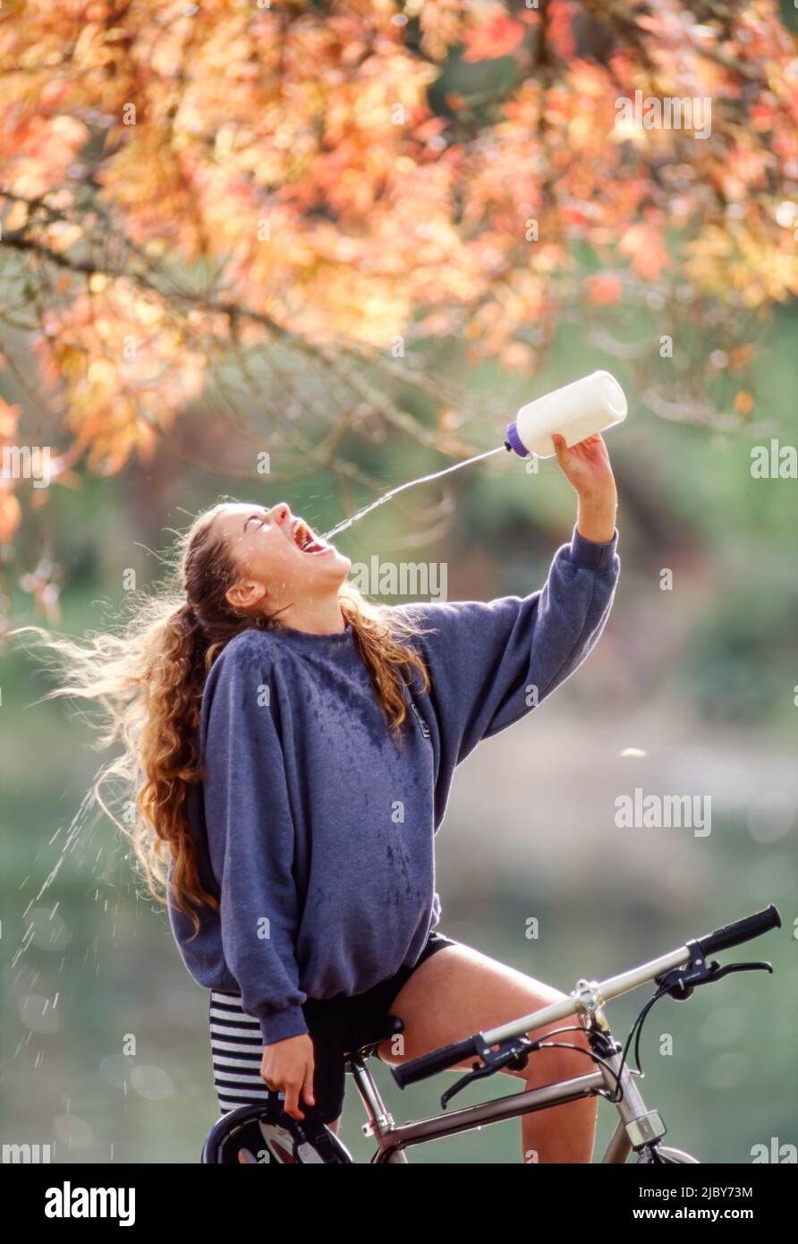 Young woman stopped on her bicycle squirting water into her mouth from ...