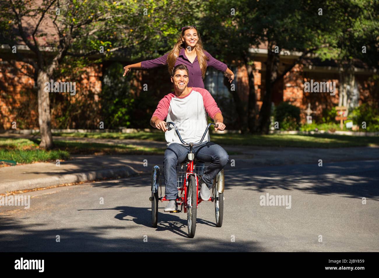 ng couple riding large tricycle through neighborhood, girl standing on ...
