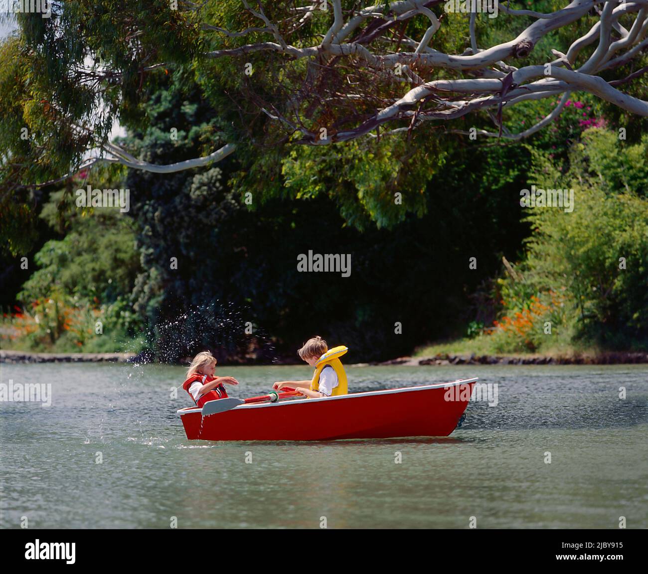 Boy rowing row boat and young sister flicking water at him from stern ...